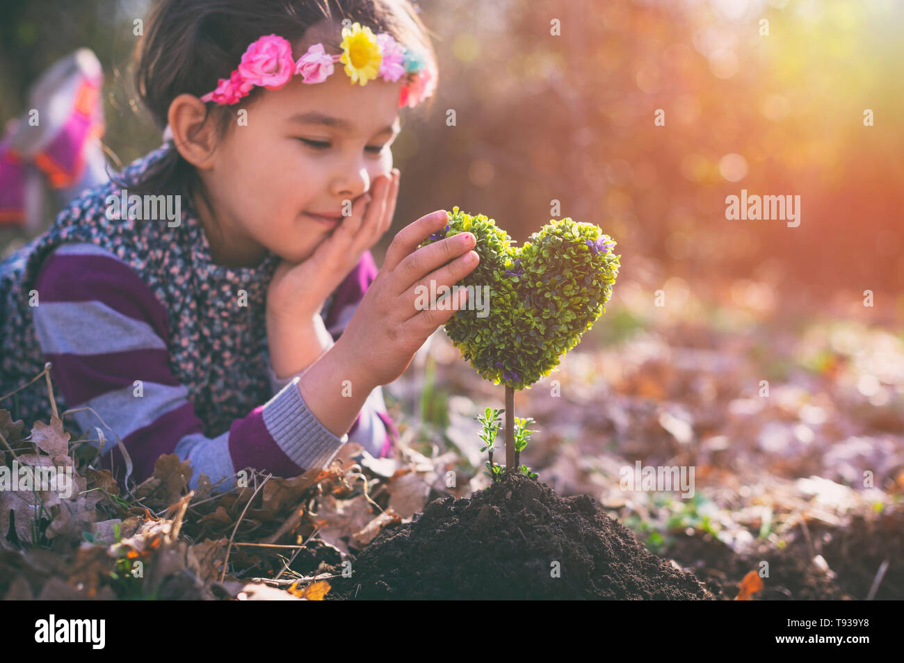 Beautiful little girl planting a heart-shaped tree and dreaming of a ...