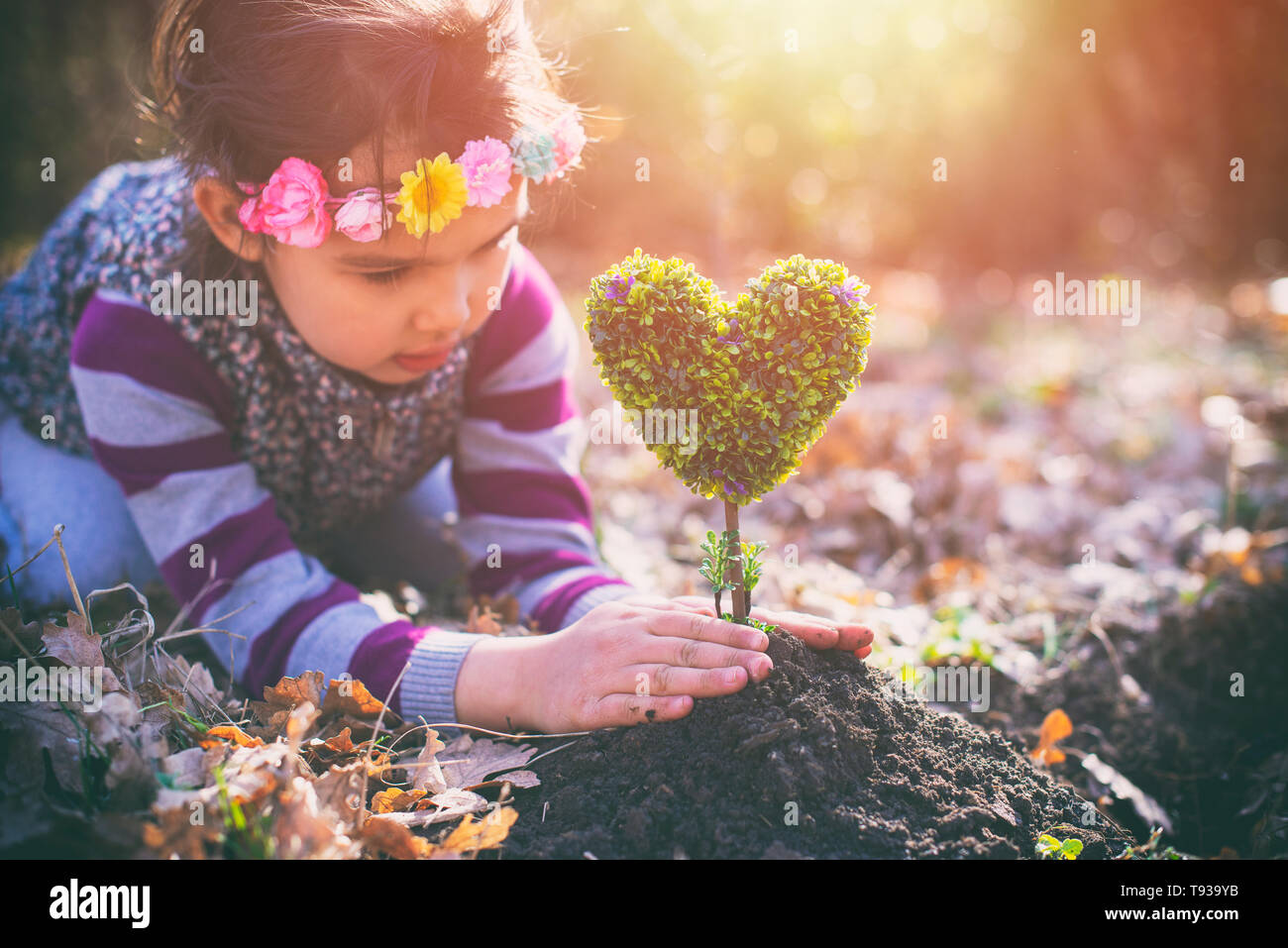 Beautiful little girl planting a heart-shaped tree and dreaming of a ...