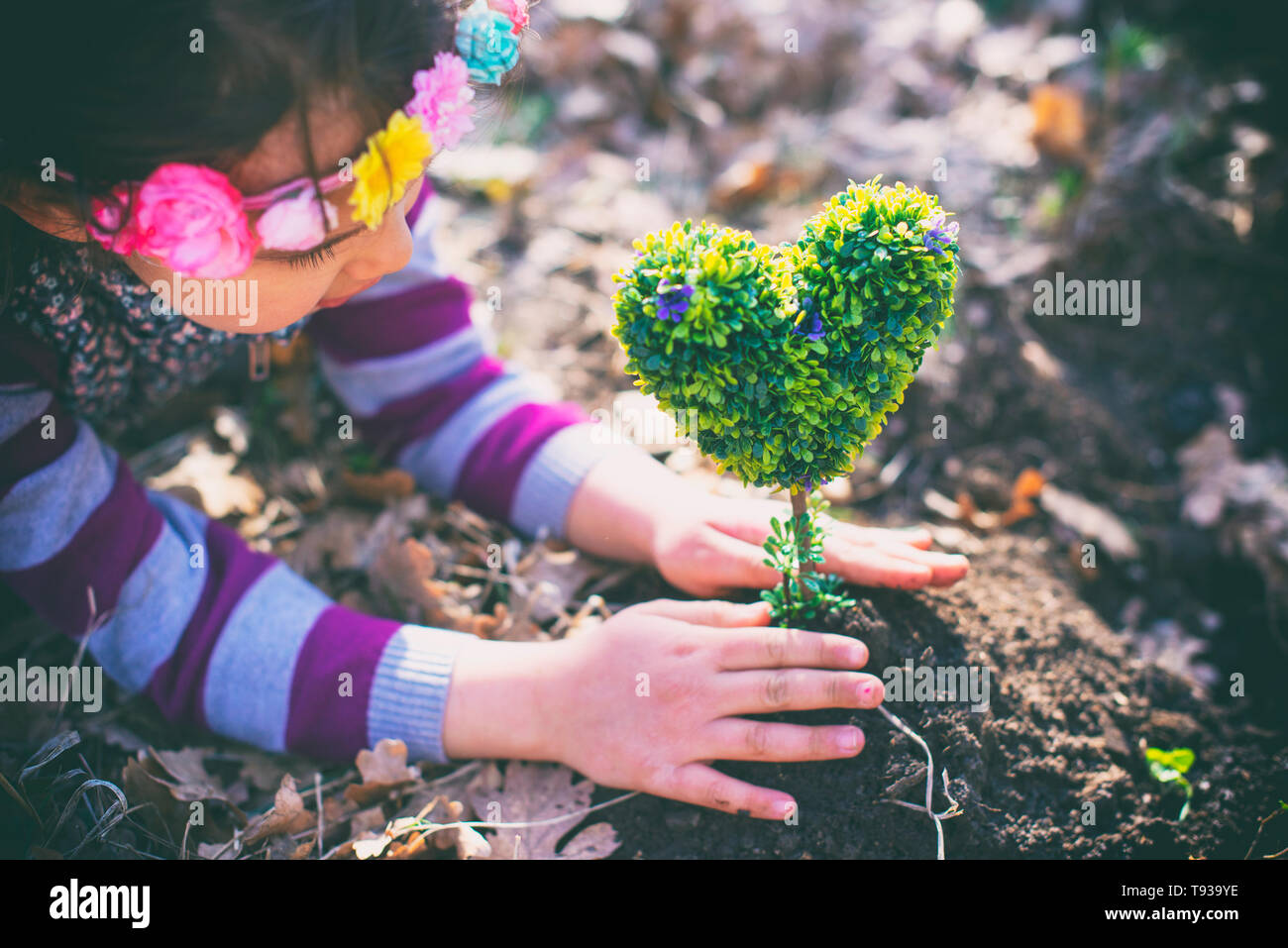 Beautiful little girl planting a heart-shaped tree and dreaming of a ...