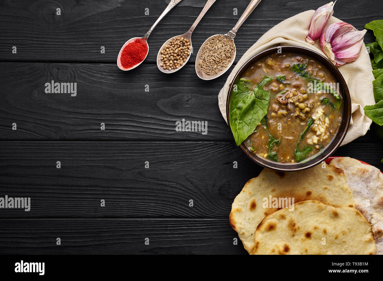 Mung Dhal, Spinach, Chapati, garlic and spices at black wooden tabletop ...