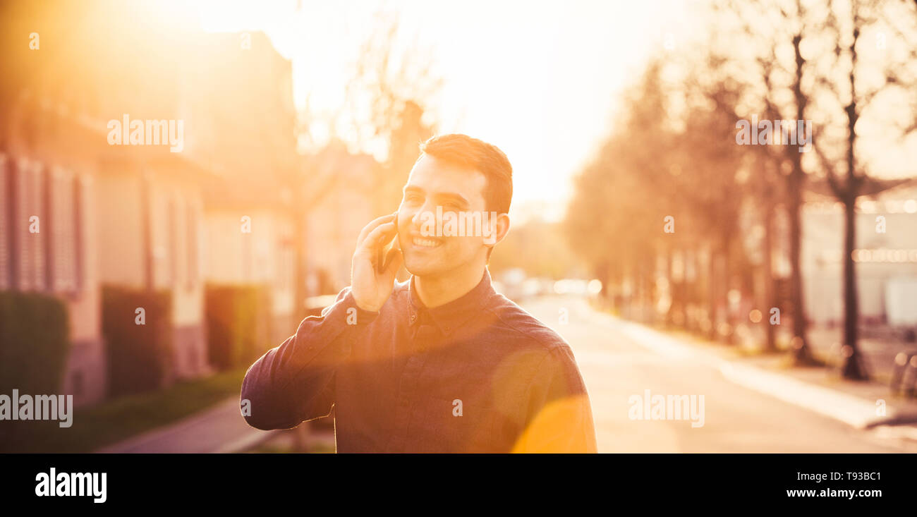 Smiling Young student man with mobile phone outdoor in sunset. Toned ...