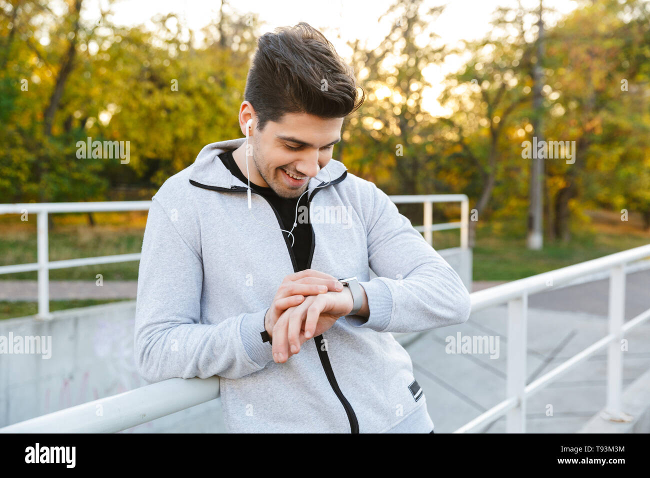 Smiling healthy sportsman standing outdoors at the railing, looking at ...