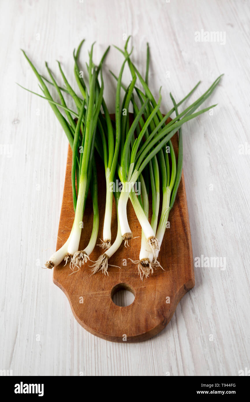 Fresh green onions on a rustic wooden board over white wooden ...