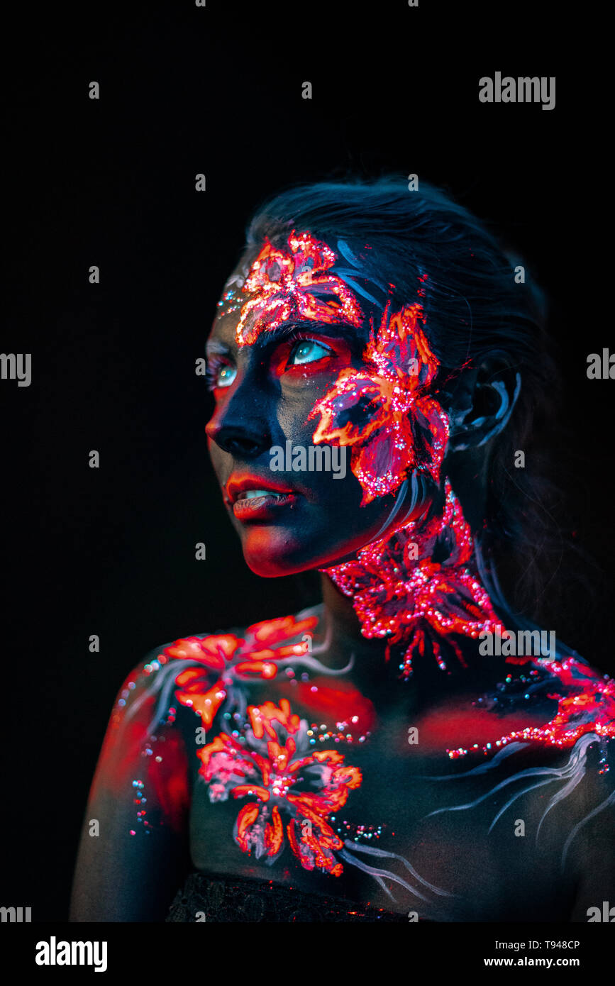 Conceptual face art with shining flowers painted in fluorescent colors ...