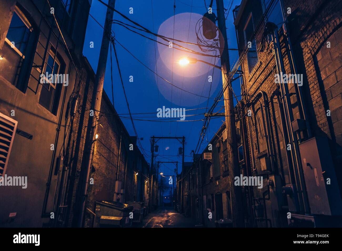 A dimly lit creepy alley with light flare and blue sky Stock Photo - Alamy