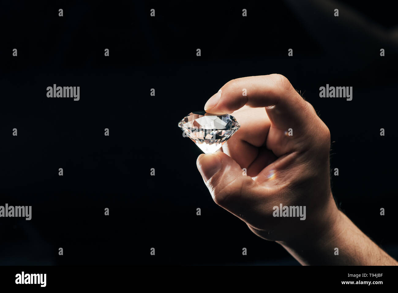 partial view of man holding big clear shiny diamond isolated on black ...