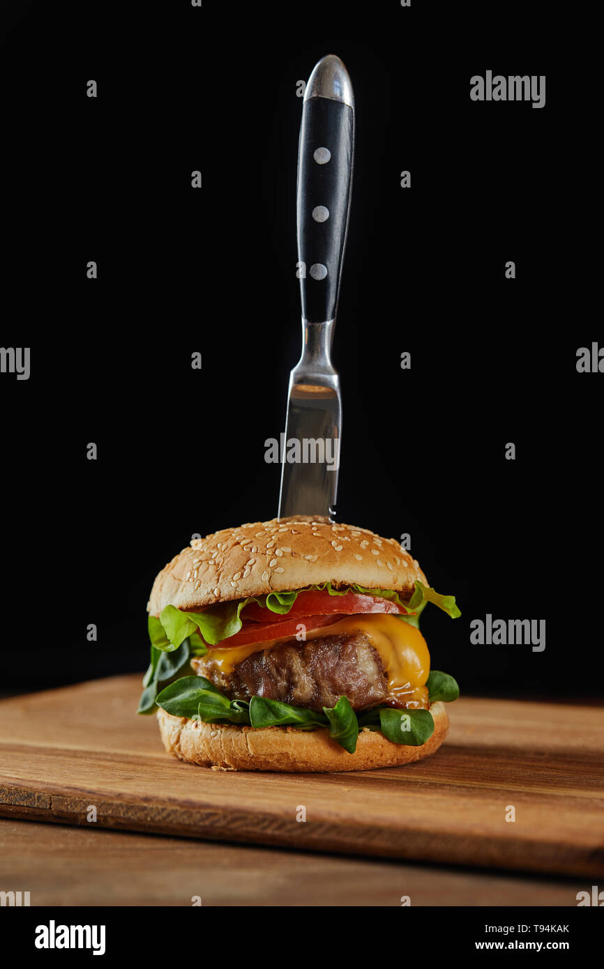 knife in delicious meat burger with cheese, greenery and tomatoes and ...