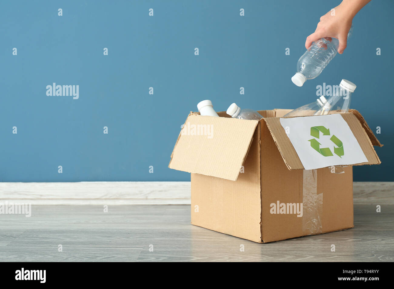 Young woman throwing plastic bottle into cardboard box indoors ...
