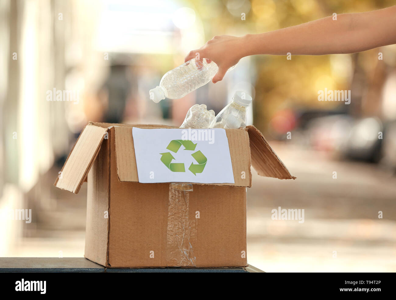 Young woman throwing plastic bottle into cardboard box outdoors ...