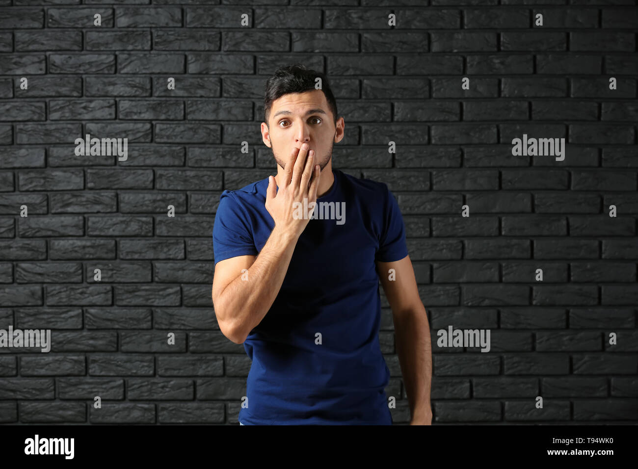Emotional young man after making mistake against dark brick wall Stock ...