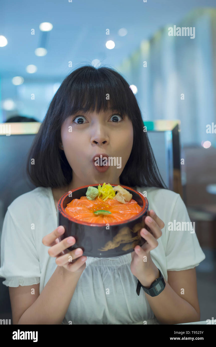 Portrait of surprised young asian woman holding japanese food dish in ...