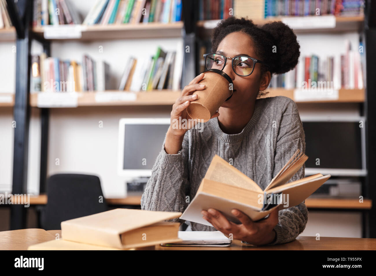 Happy young african student girl studying at the library, reading a ...