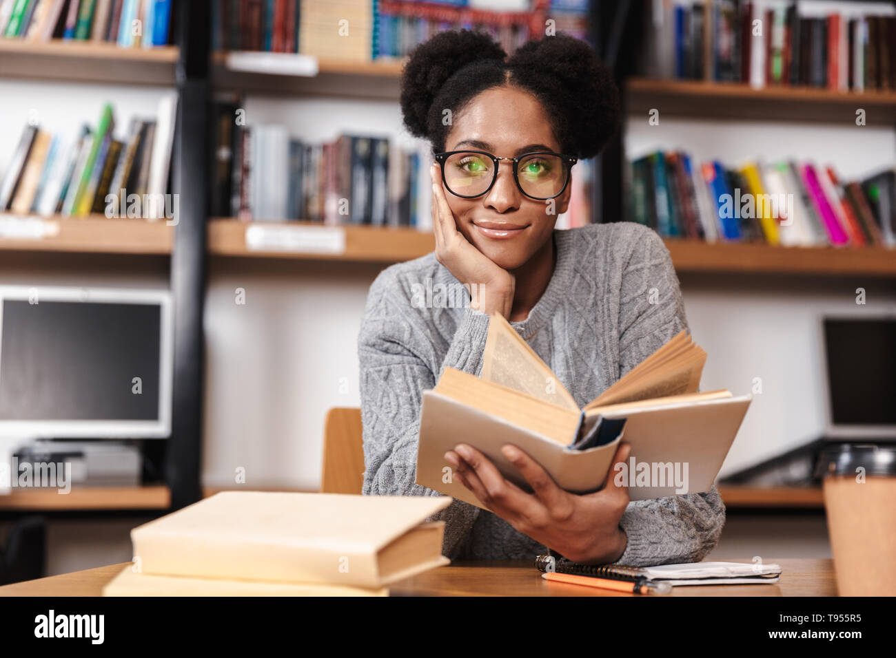 Happy young african student girl studying at the library, reading a ...