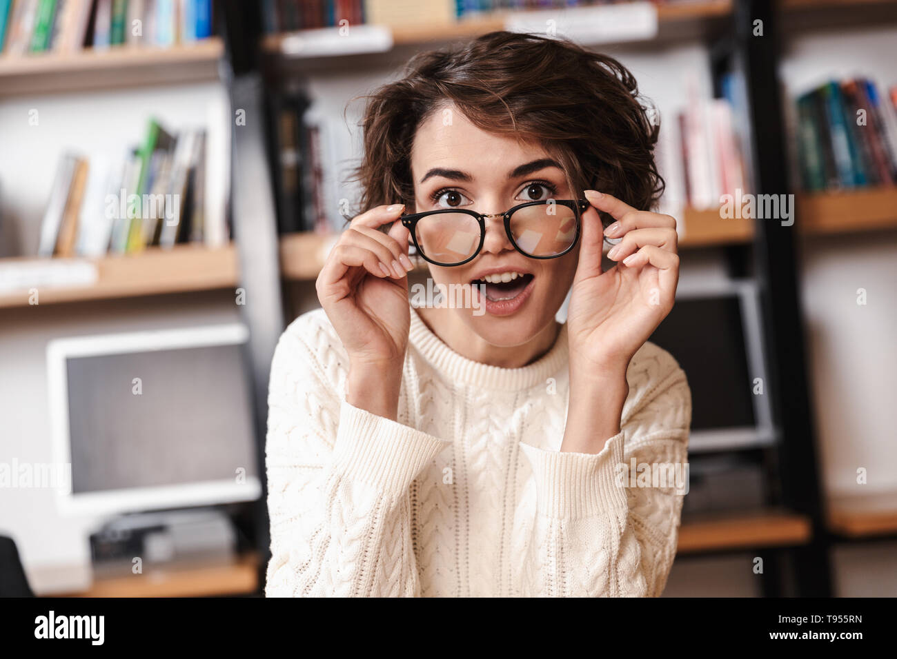 Smiling young student girl studying while sitting at the library desk ...
