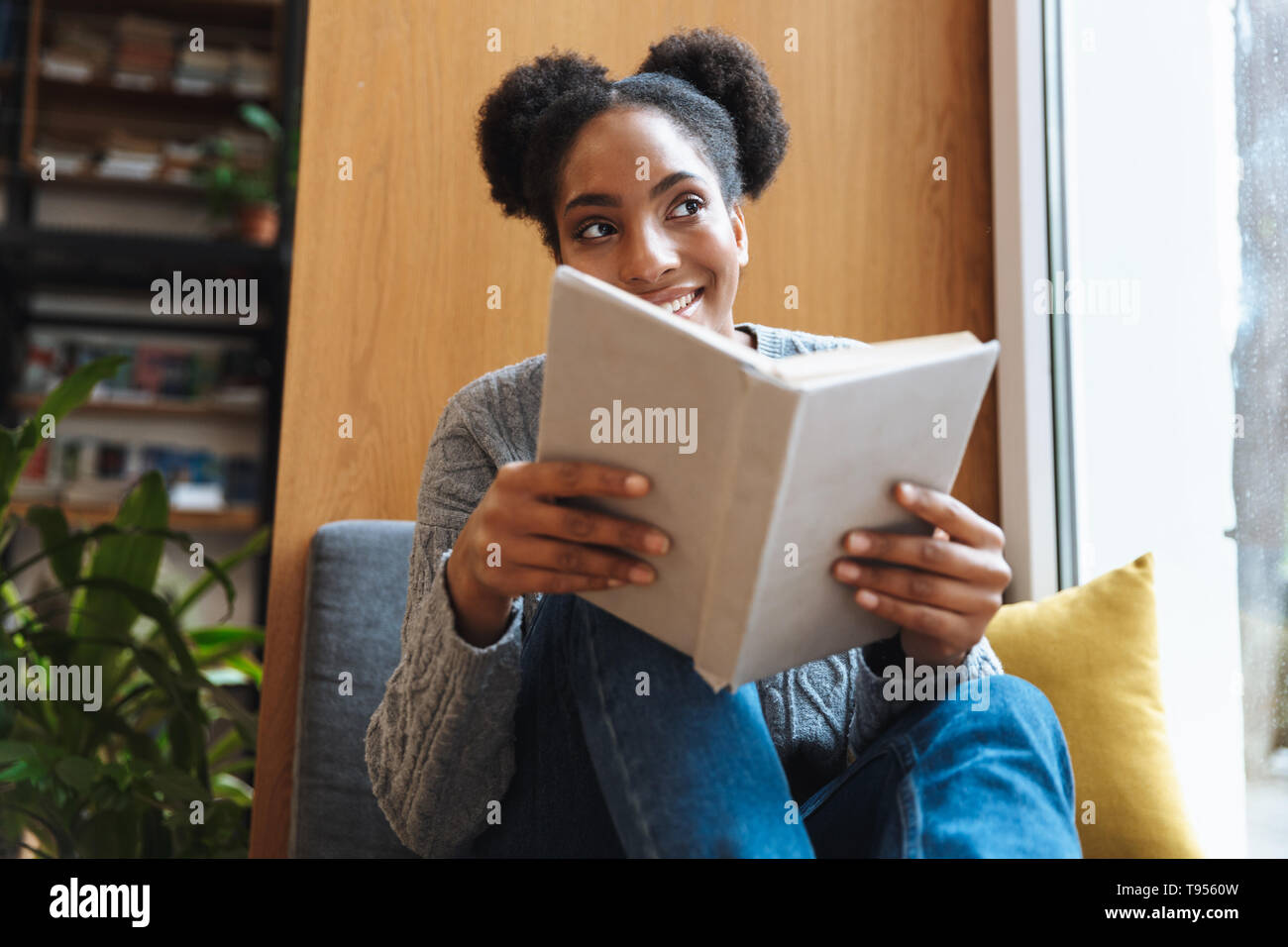 Happy young african student girl studying at the library, reading a ...