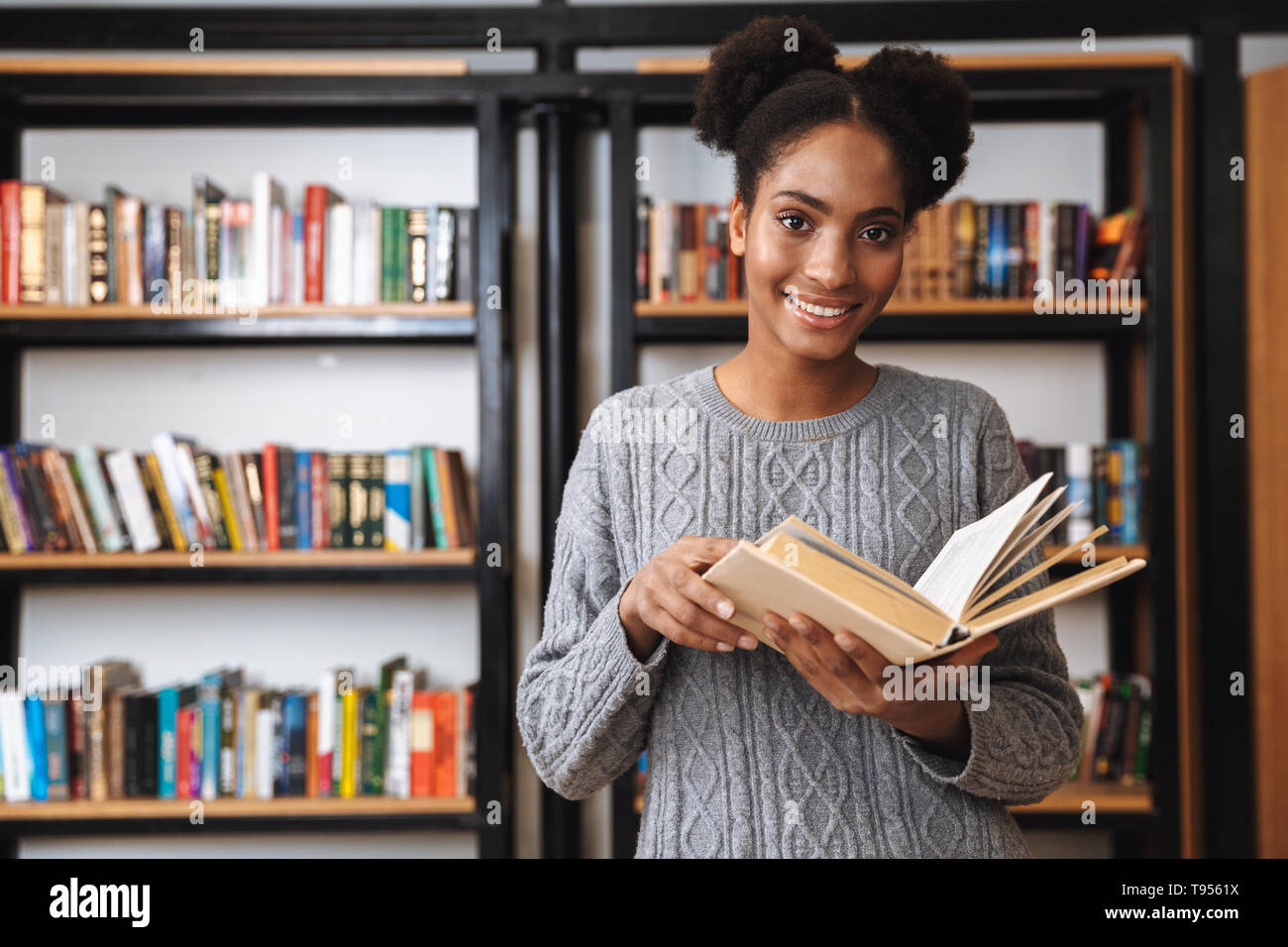 Happy young african student girl studying at the library, reading a ...