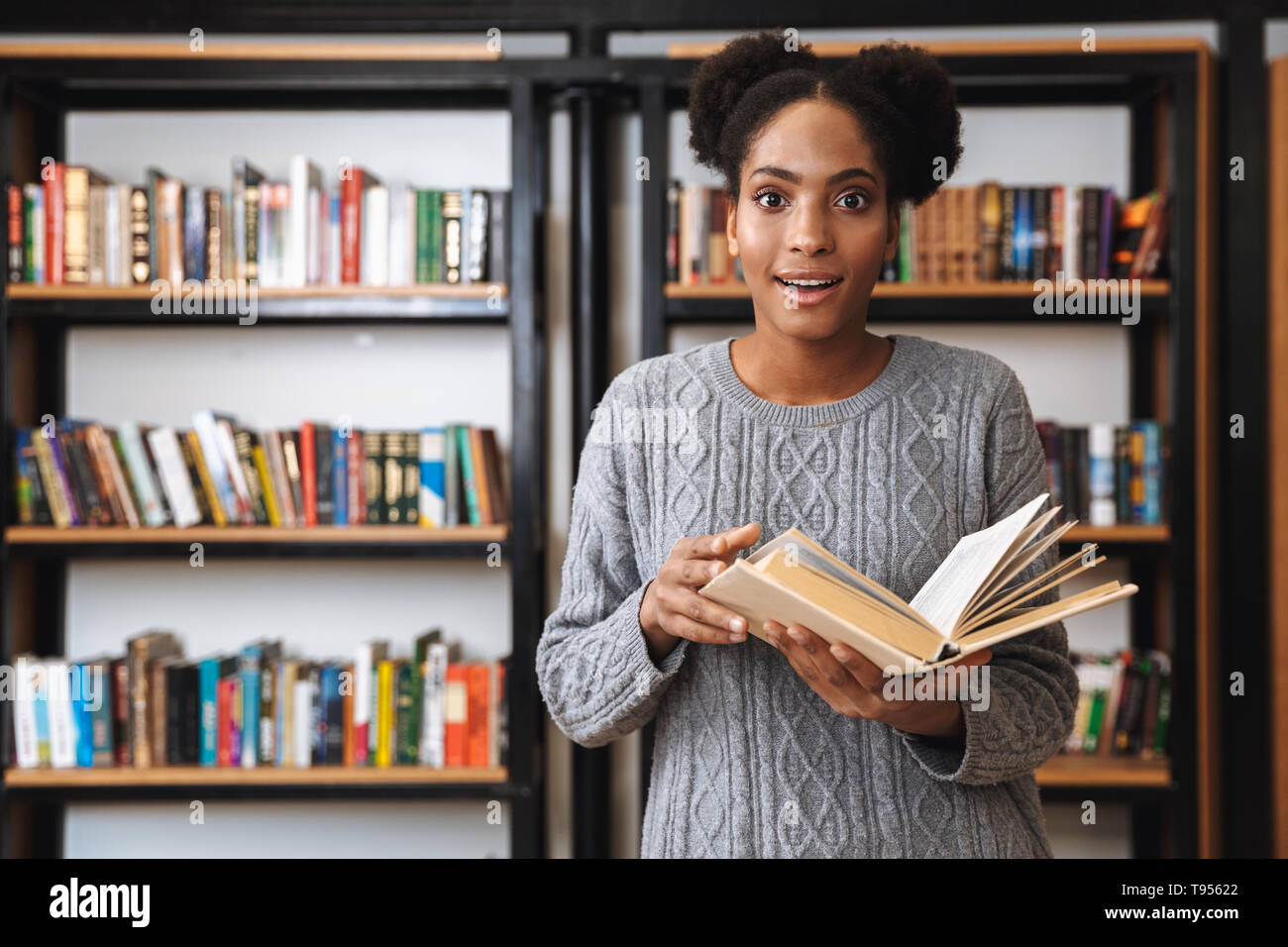 Happy young african student girl studying at the library, reading a ...
