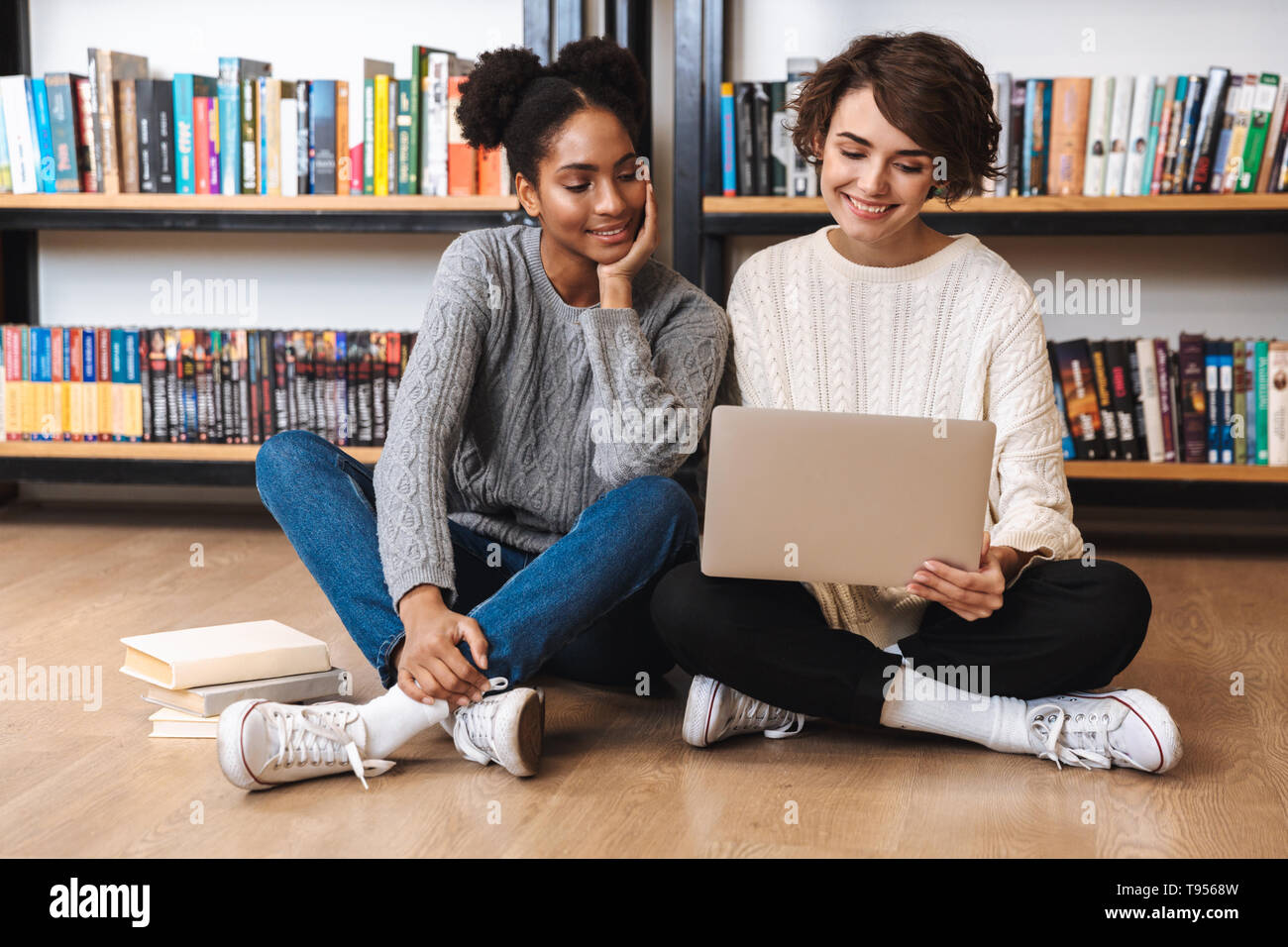Two cheerful young girls students studying at library, sitting on a ...