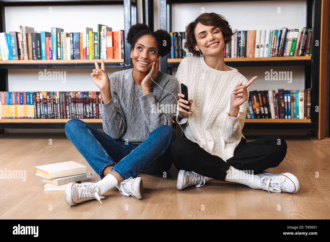 Two cheerful young girls students studying at library, sitting on a ...