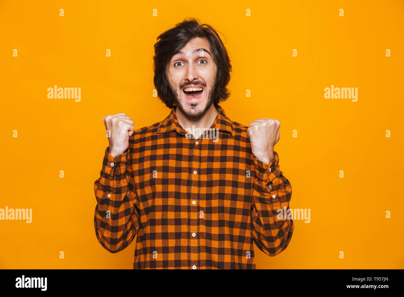 Portrait of happy man wearing plaid shirt rejoicing and clenching fists ...
