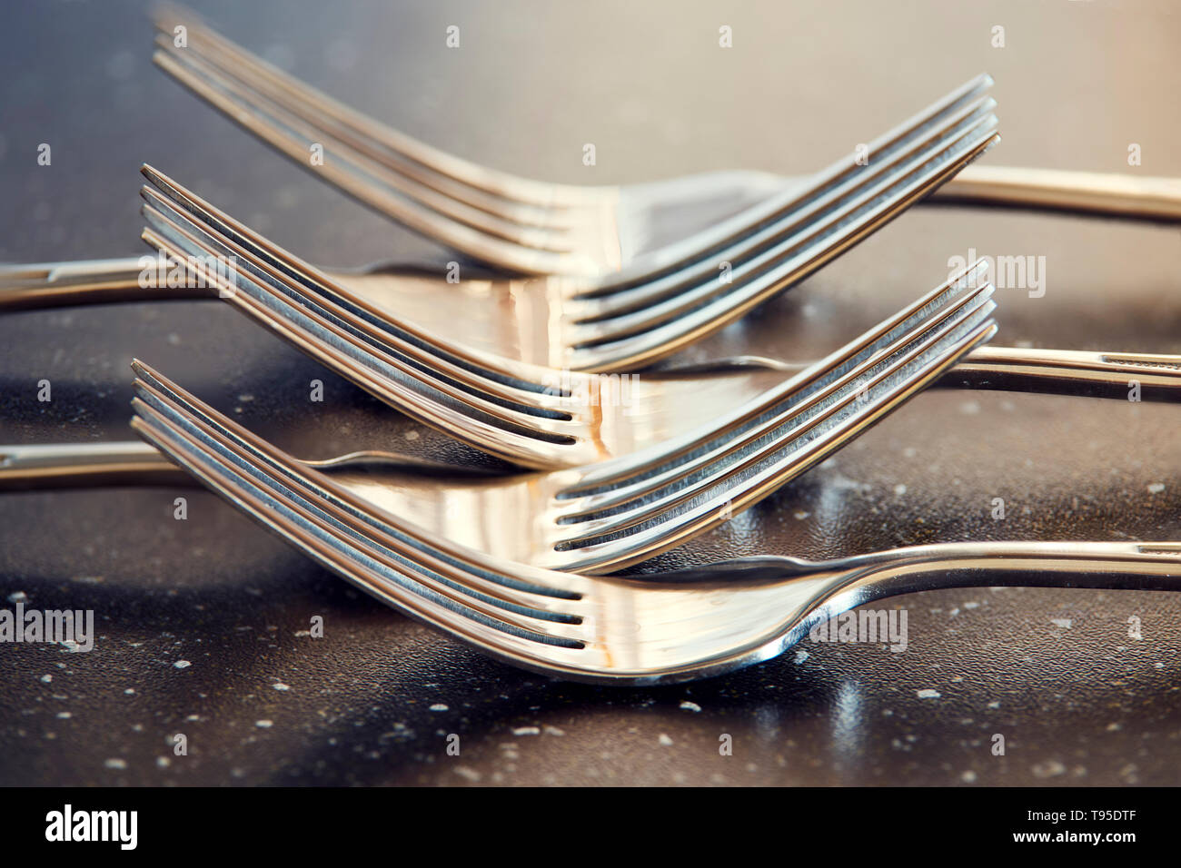 Crossed five steel forks on black table. Macro photography for dishware ...