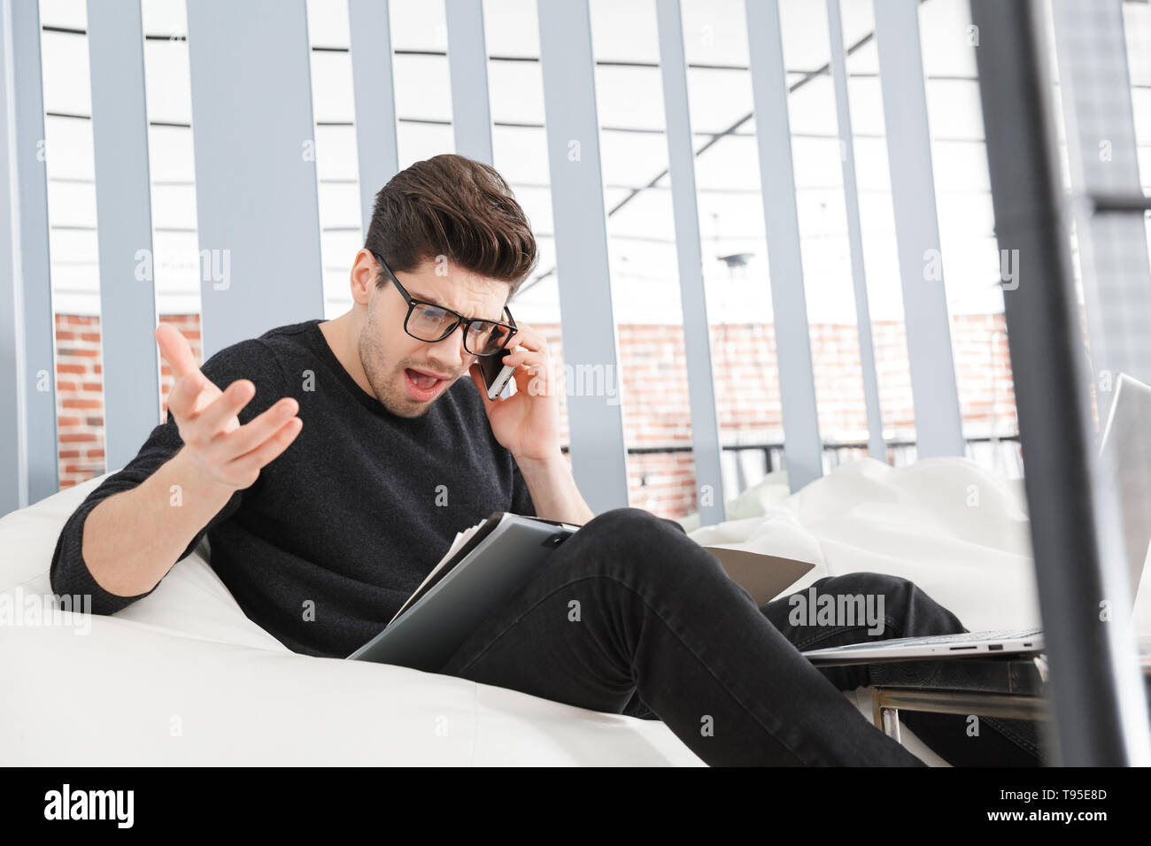 Angry young business man working at the office while sitting in a couch ...