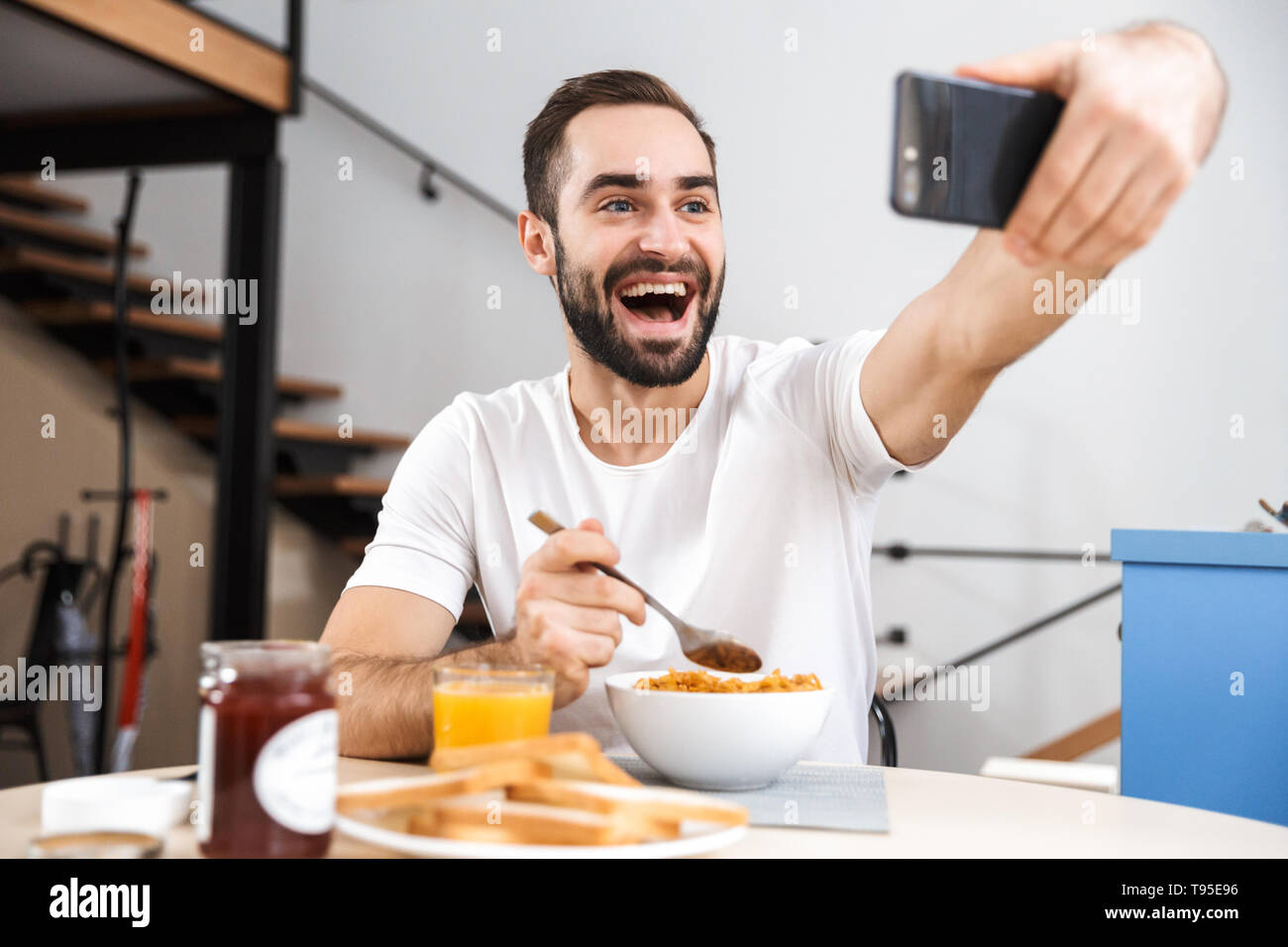 Handsome young man having breakfast while sitting at the kitchen ...