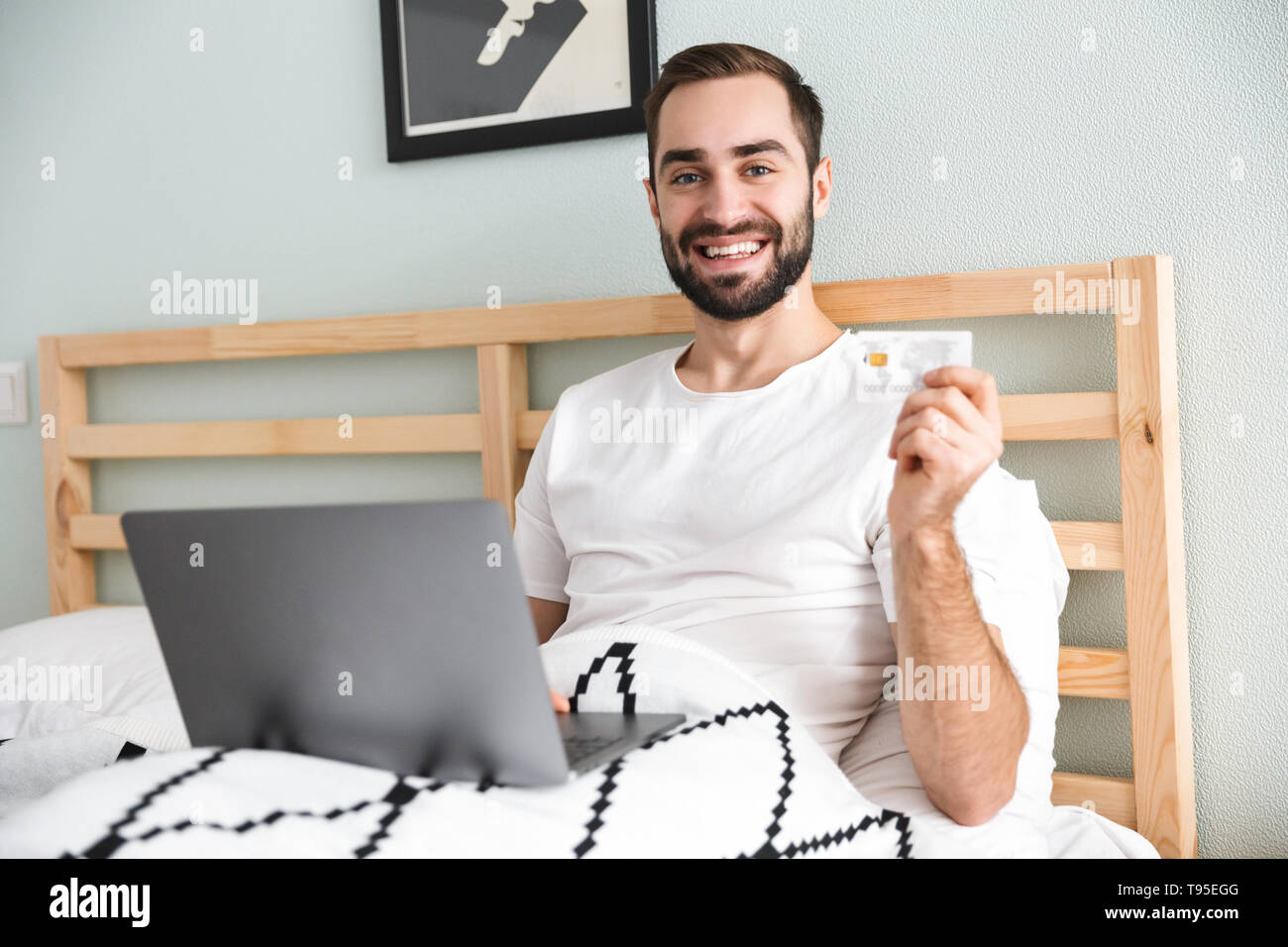 Handsome young man laying in bed, working on laptop computer, showing ...