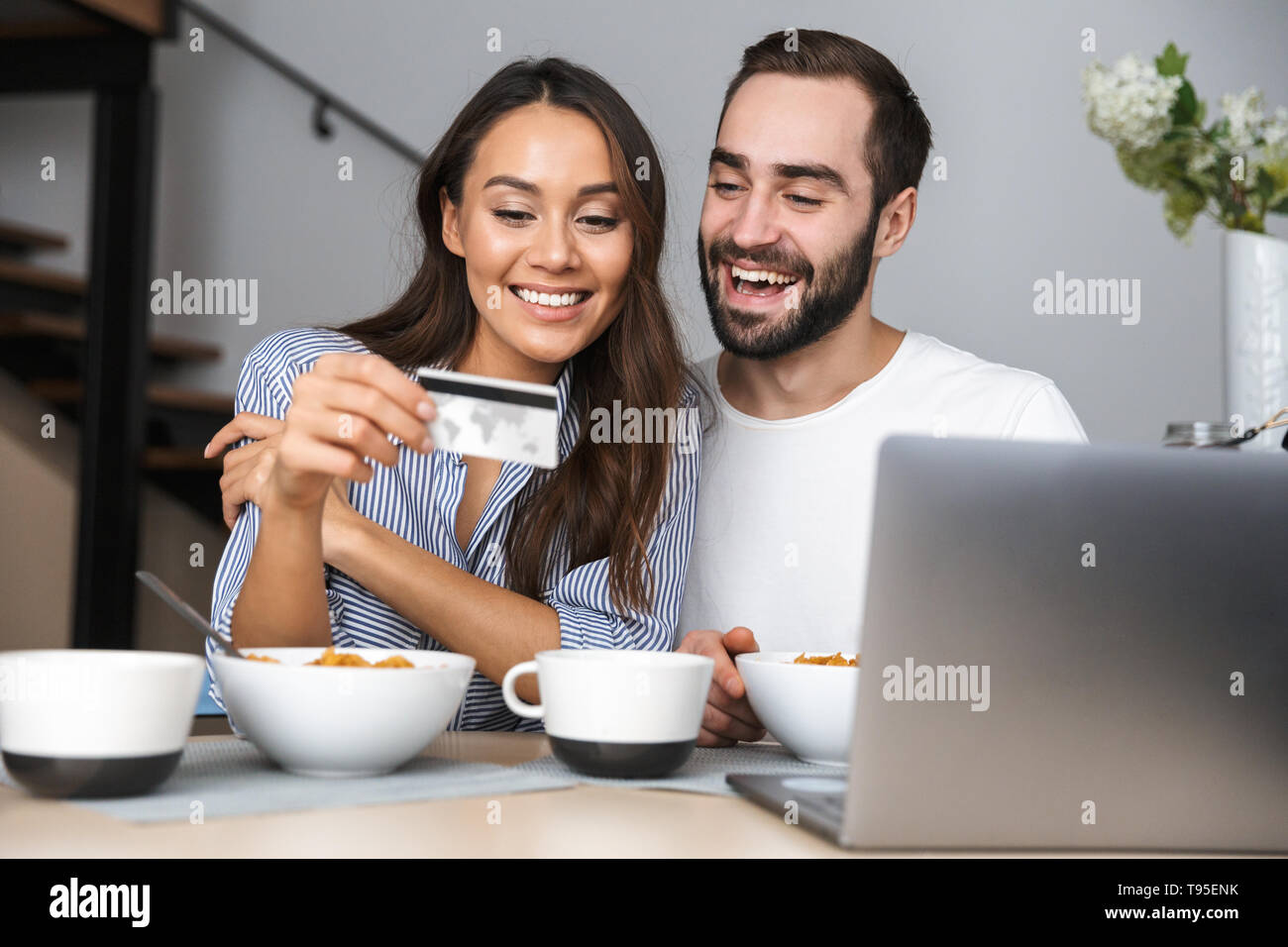 Happy multiethnic couple having breakfast at the kitchen, looking at ...