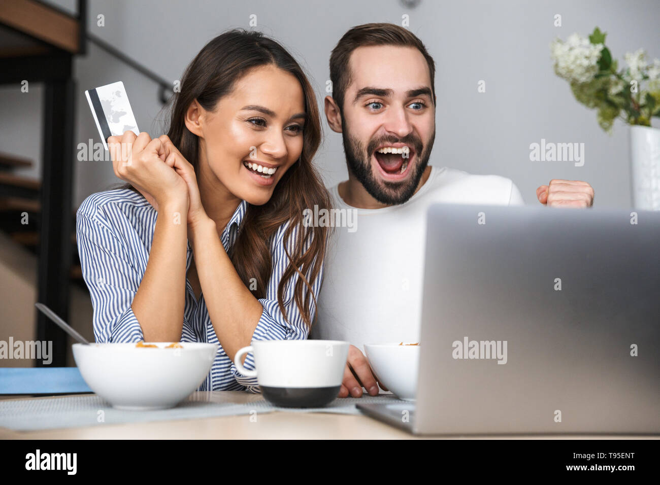 Happy multiethnic couple having breakfast at the kitchen, looking at ...