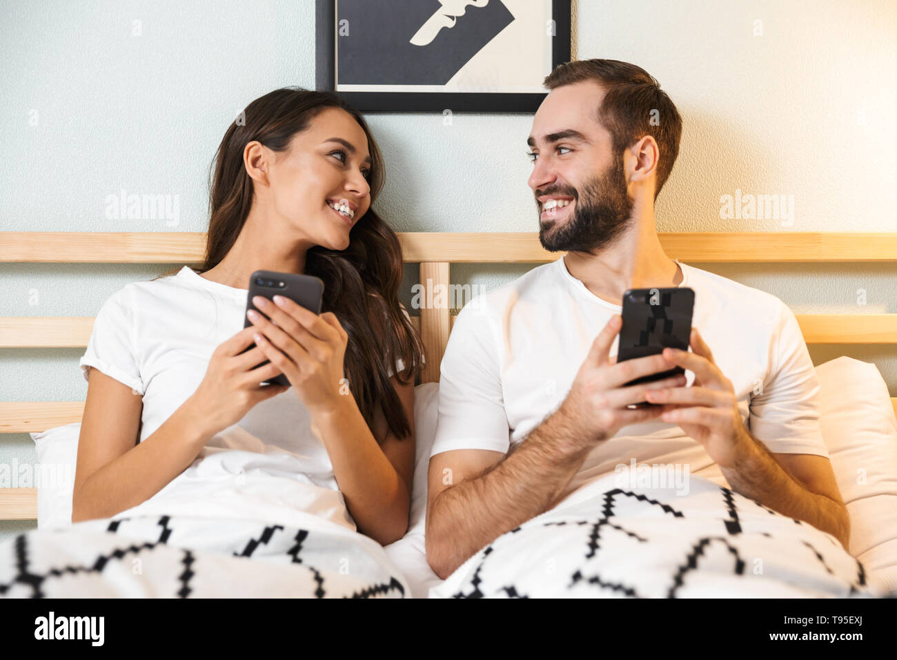 Smiling young couple laying in bed, using mobile phones Stock Photo - Alamy