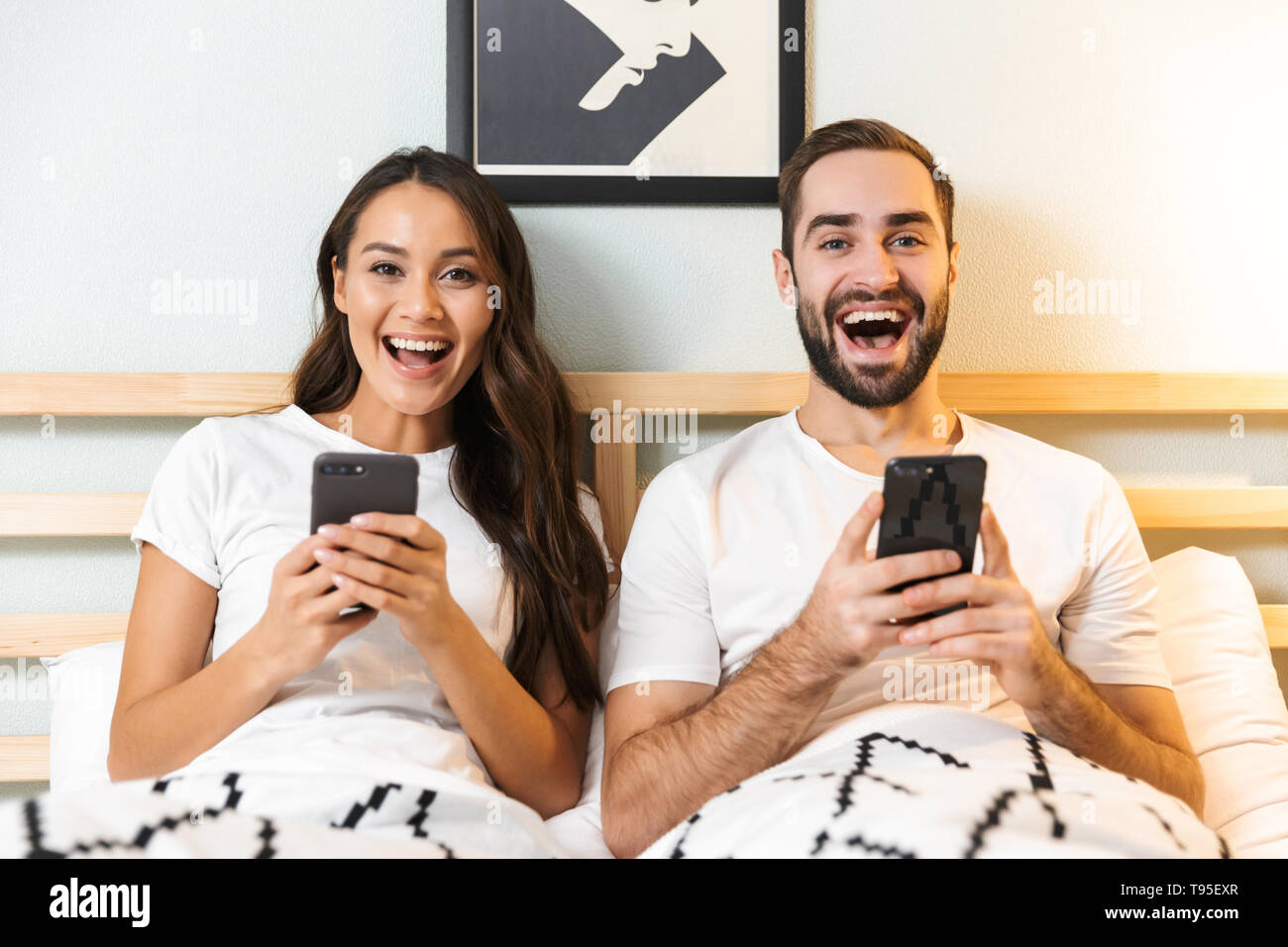 Smiling young couple laying in bed, using mobile phones Stock Photo - Alamy