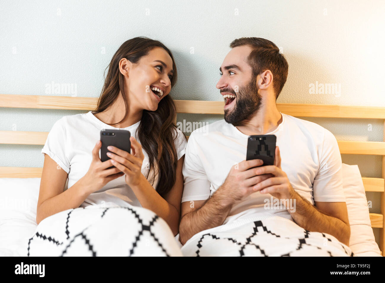 Beautiful young couple laying together in bed in the morning, using ...