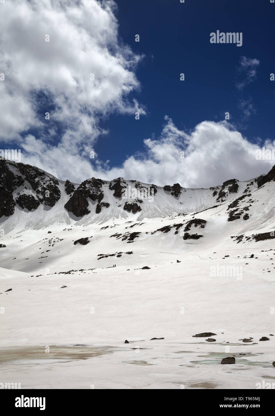 Frozen lake covered with snow, sunlit mountain pass and blue cloudy sky ...