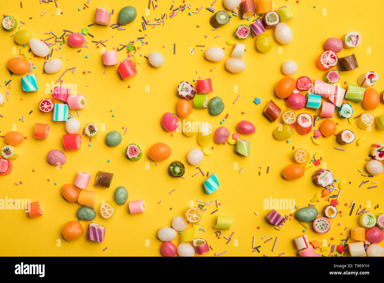 top view of multicolored candies and sprinkles scattered on yellow ...