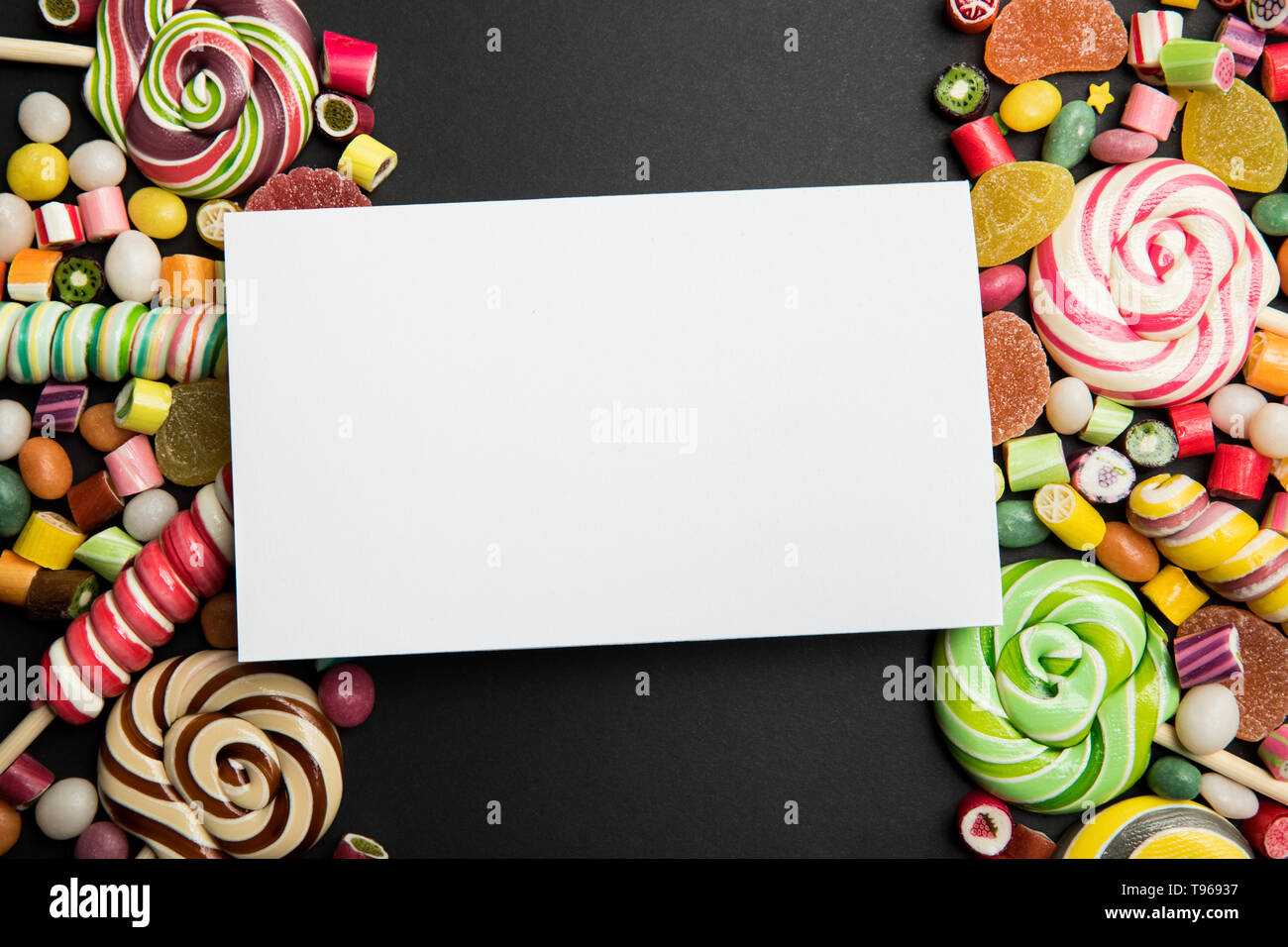 top view of delicious multicolored sweets and blank white card on black ...