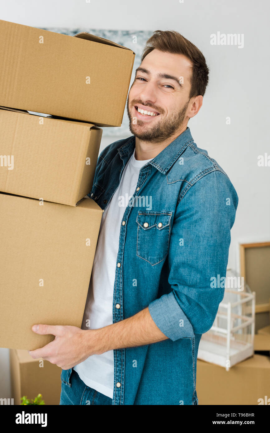 Joyful man in denim jacket holding cardboard boxes and looking at ...