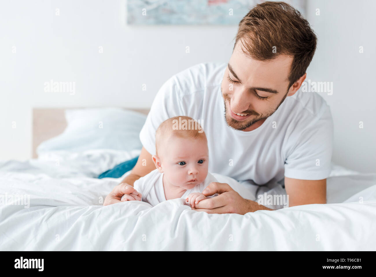 Smiling father lying on bed with baby in bedroom Stock Photo - Alamy