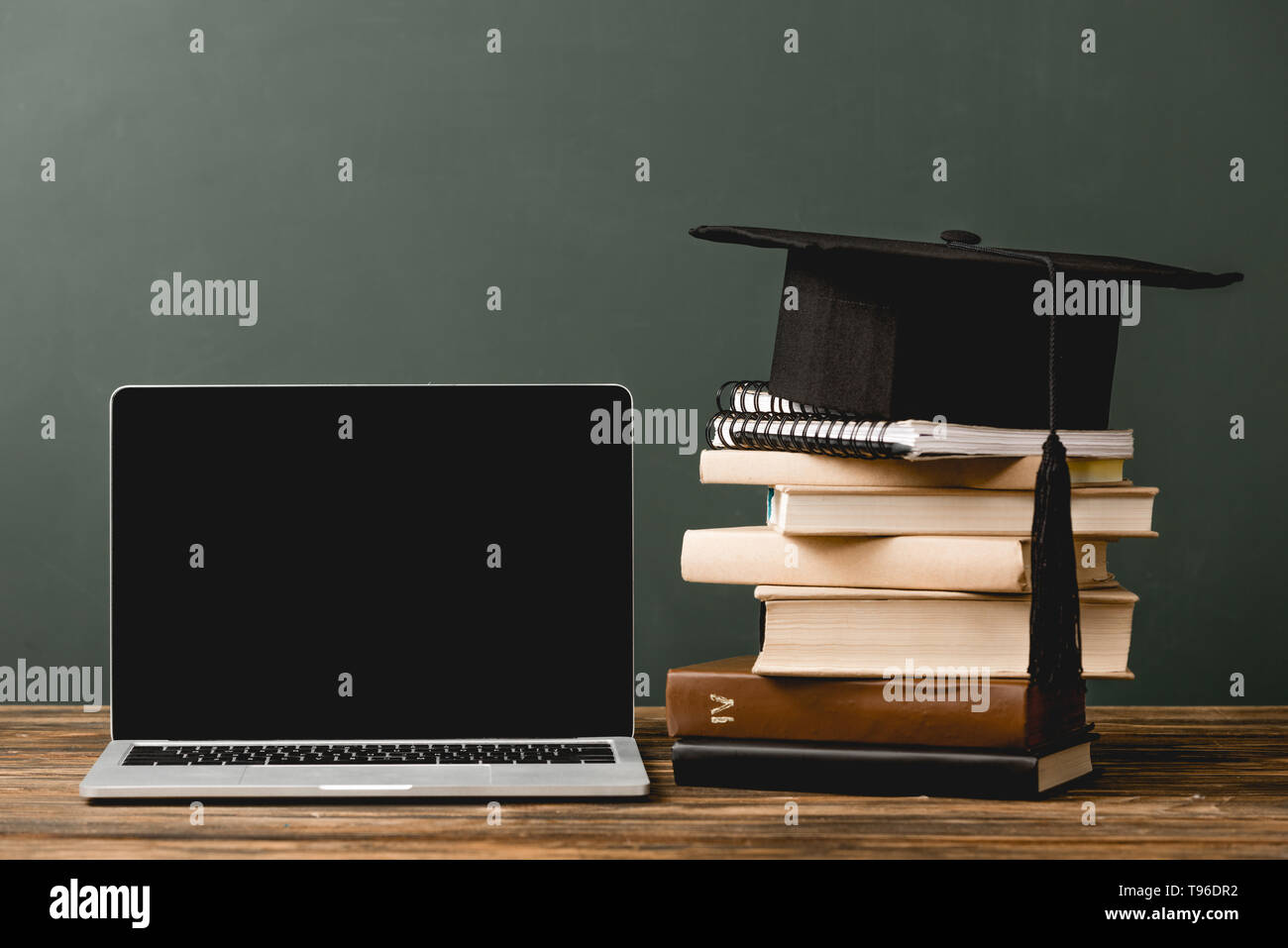 books, notebooks, academic cap and laptop with blank screen on wooden ...