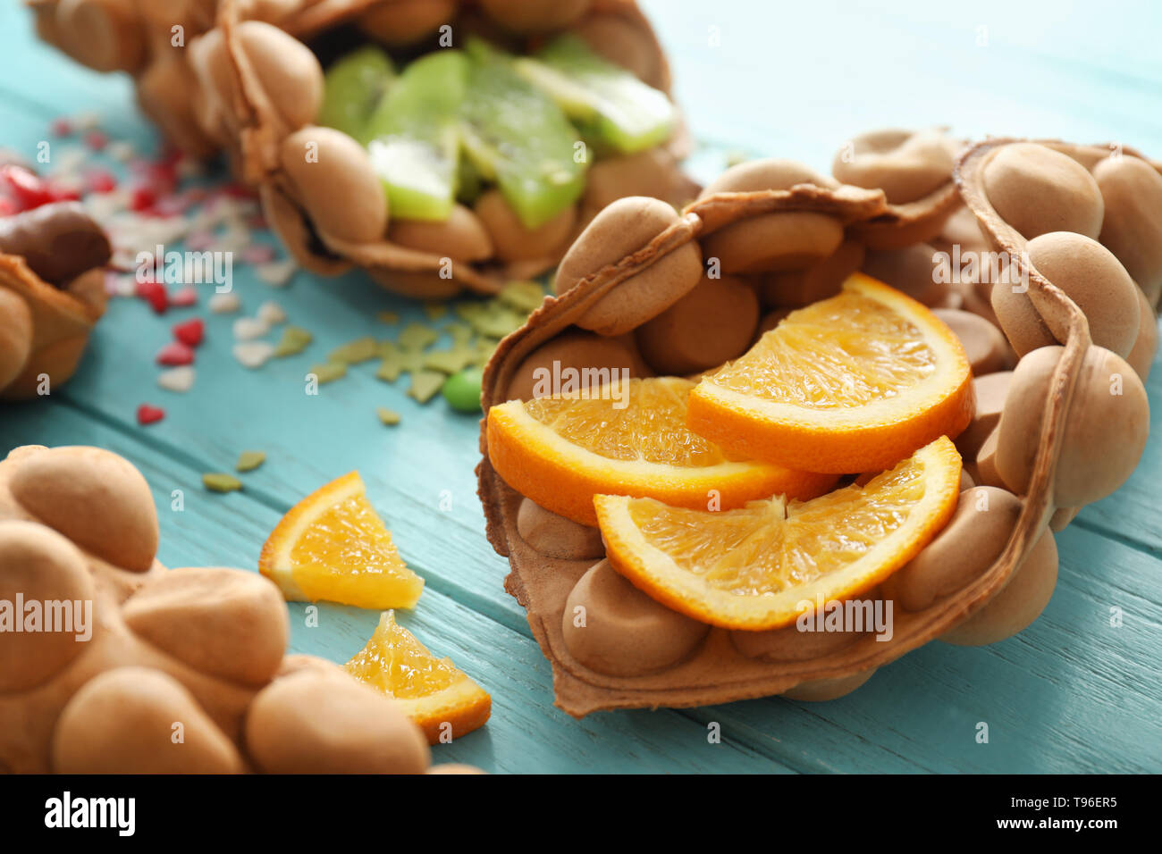 Delicious sweet bubble waffle with orange slices on color wooden table ...