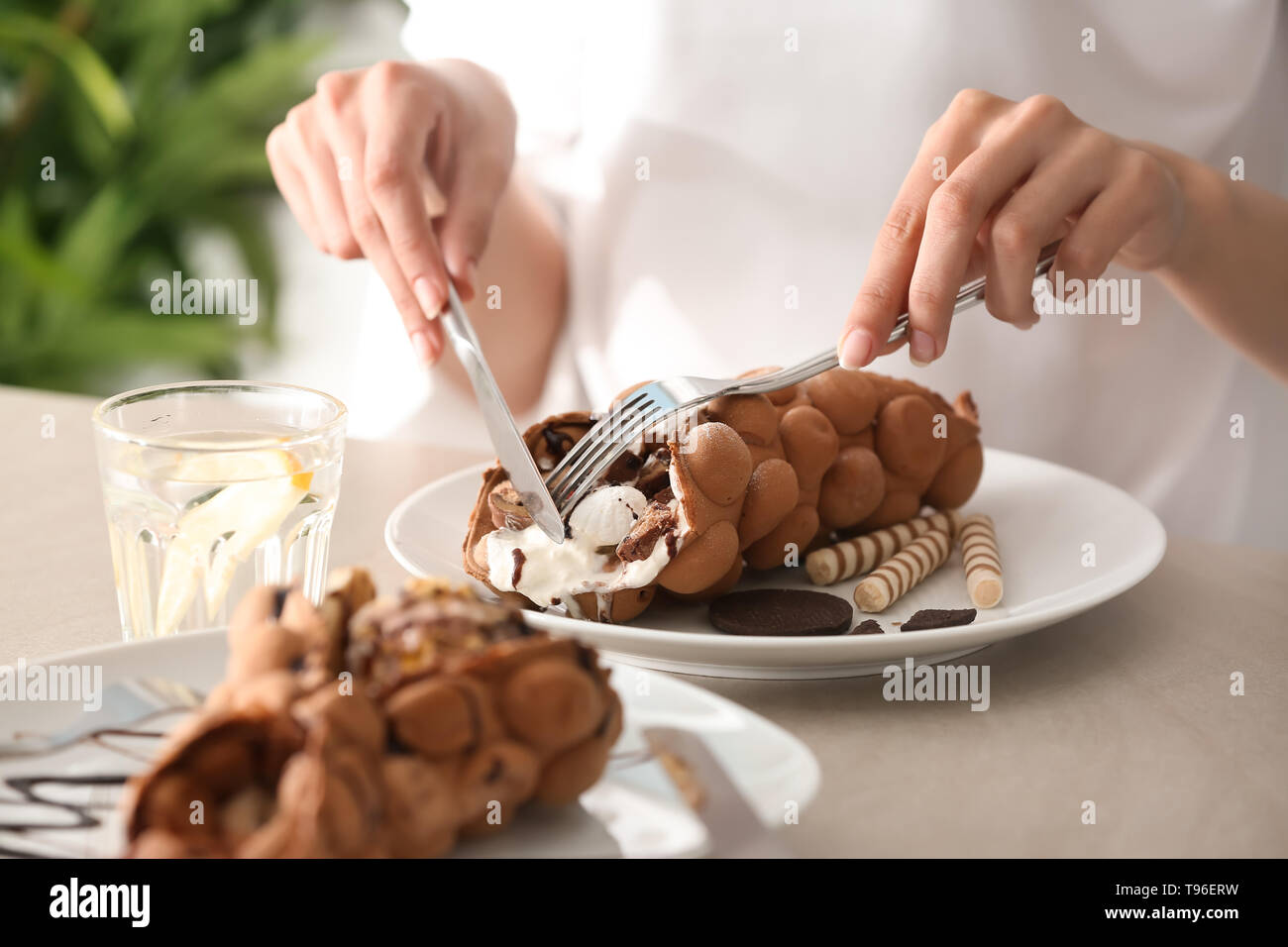 Woman eating sweet bubble waffle at table Stock Photo - Alamy