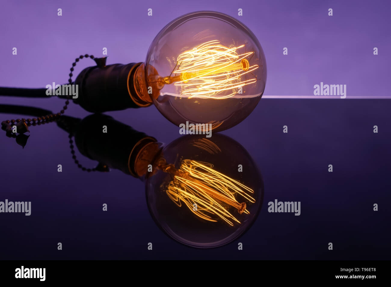 Glowing retro light bulb with reflection on color table Stock Photo - Alamy