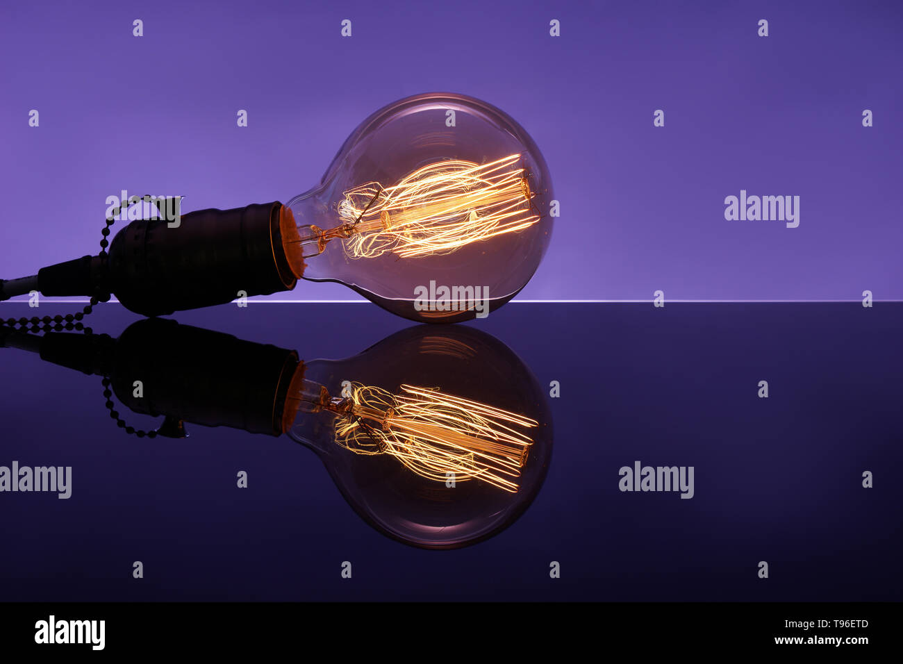 Glowing retro light bulb with reflection on color table Stock Photo - Alamy