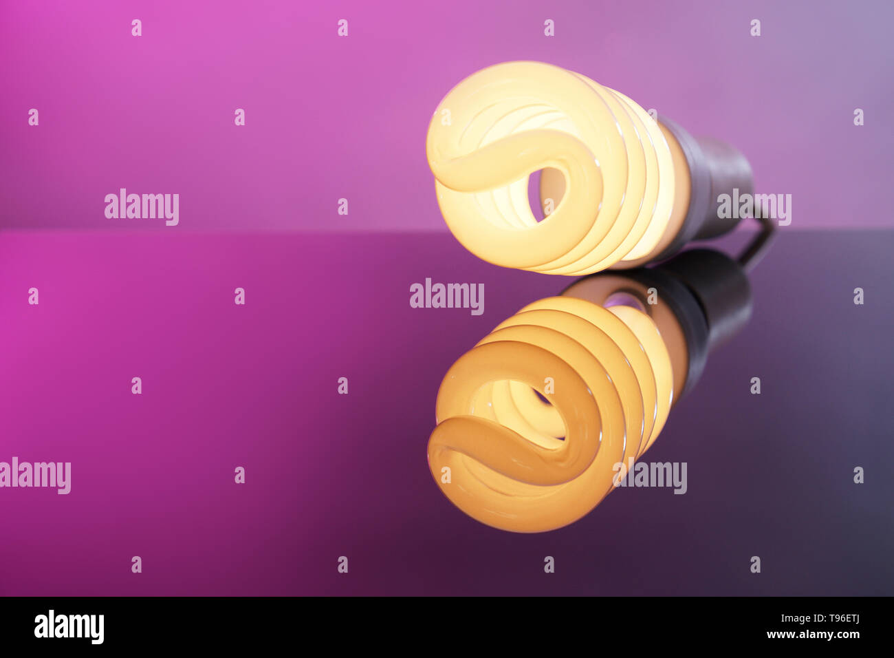 Glowing spiral light bulb with reflection on color table Stock Photo ...