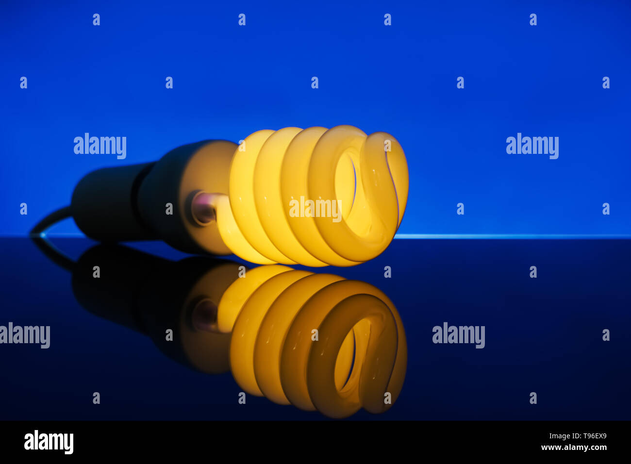 Glowing spiral light bulb with reflection on color table Stock Photo ...