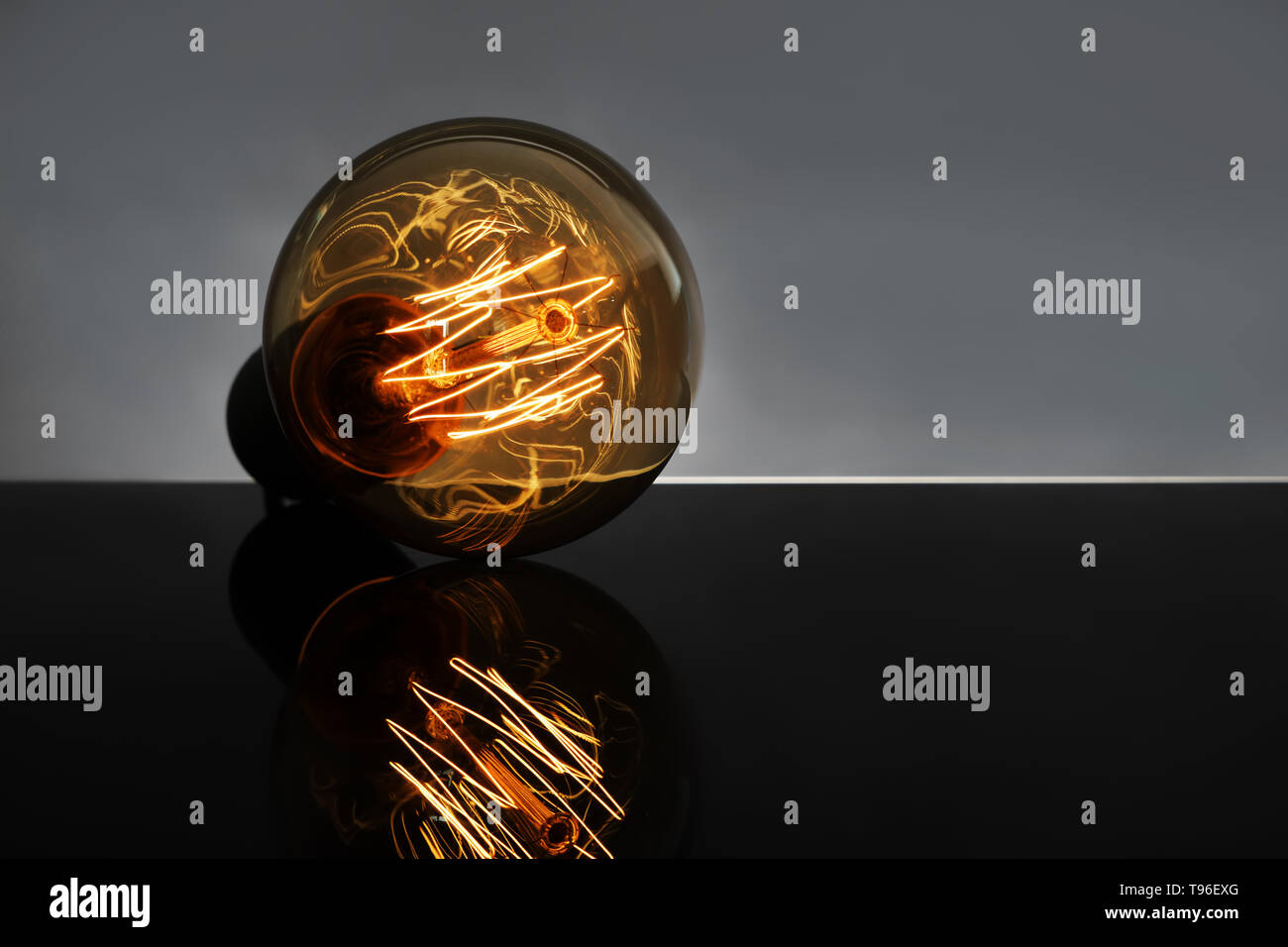 Glowing retro light bulb with reflection on dark table Stock Photo - Alamy