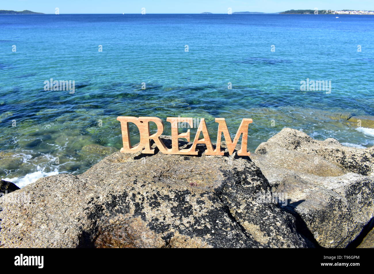 Coast with Dream wooden sign on the rocks. Blue sea, sunny day. Rias ...