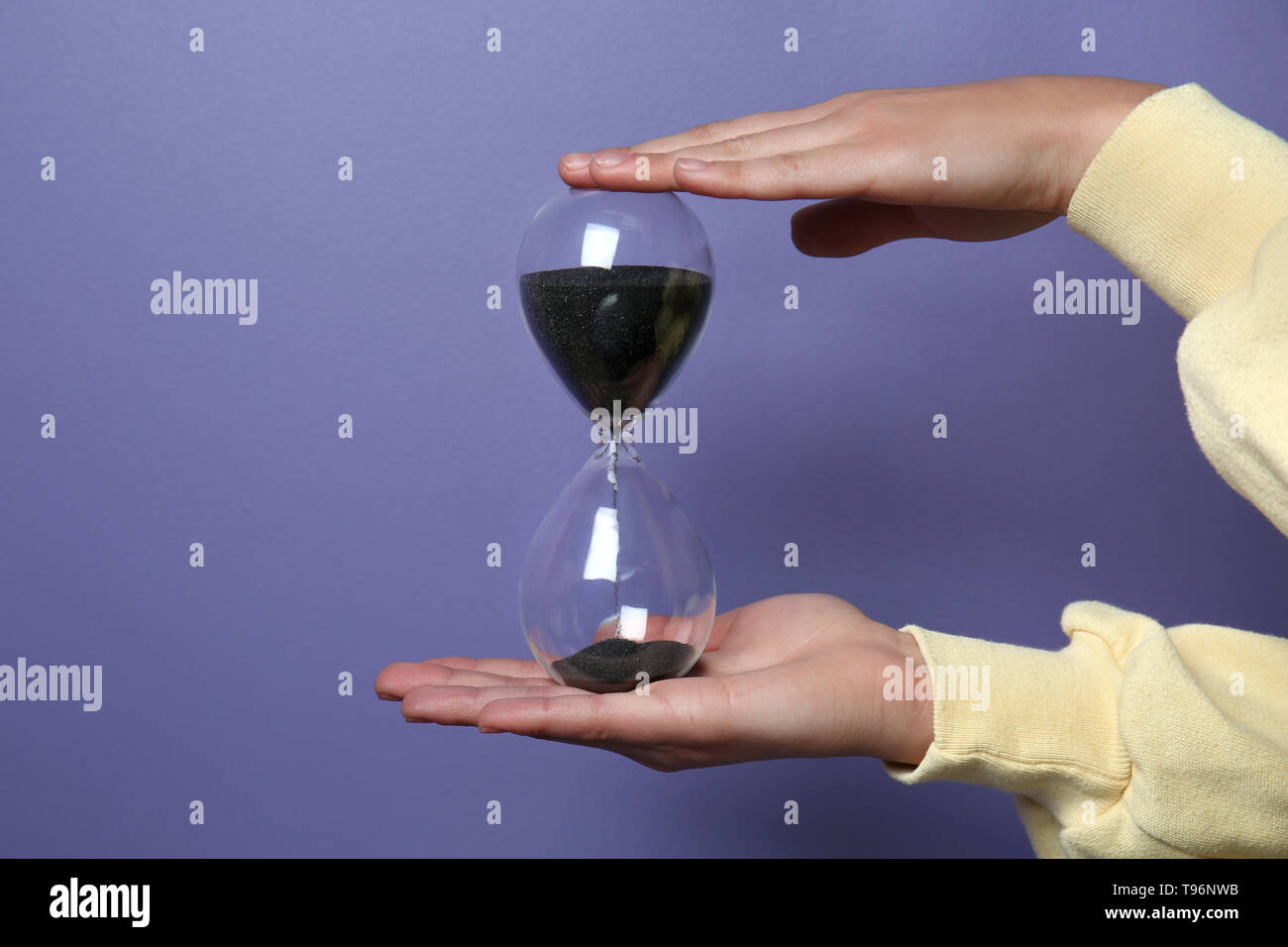 Female hands holding hourglass on color background Stock Photo - Alamy