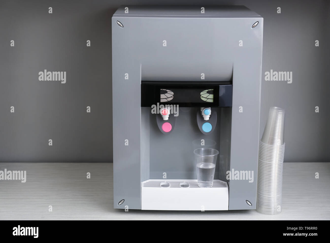 Modern water cooler with plastic cups on white table Stock Photo - Alamy