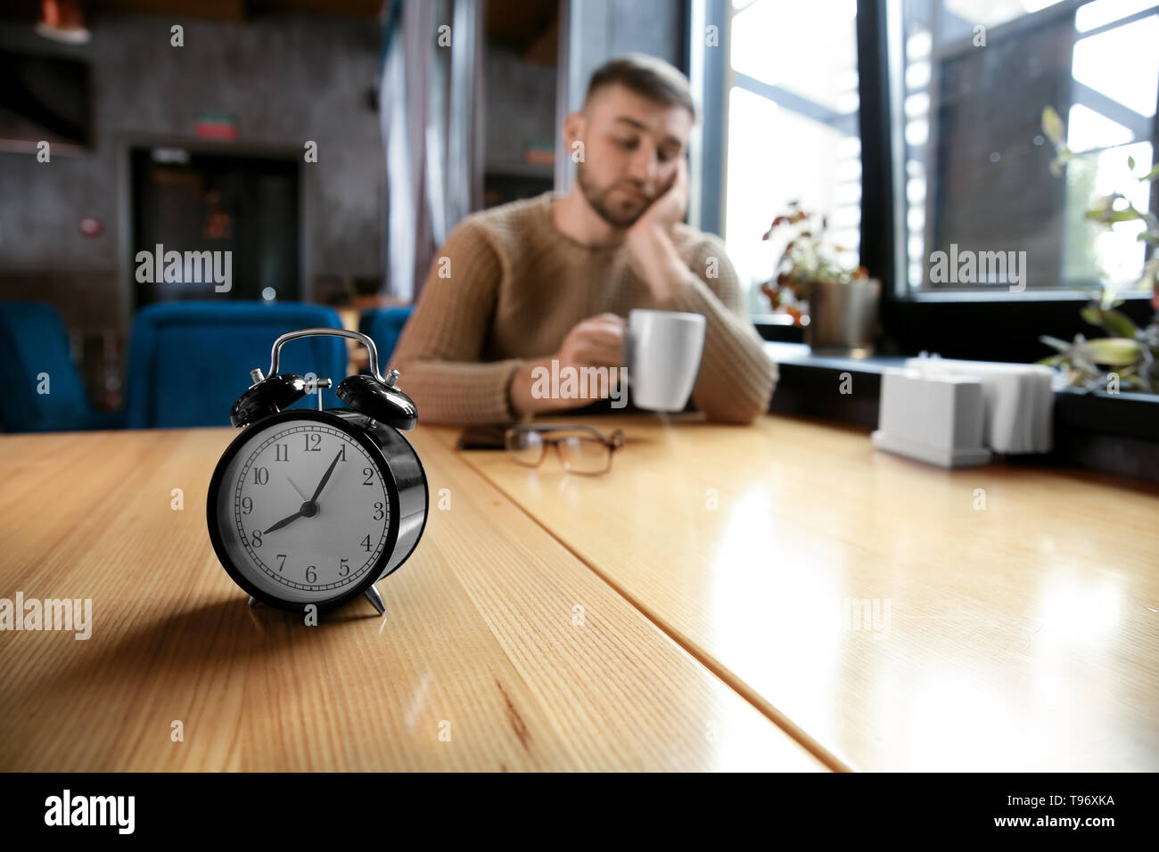 Alarm clock on table of bored young man in cafe Stock Photo - Alamy